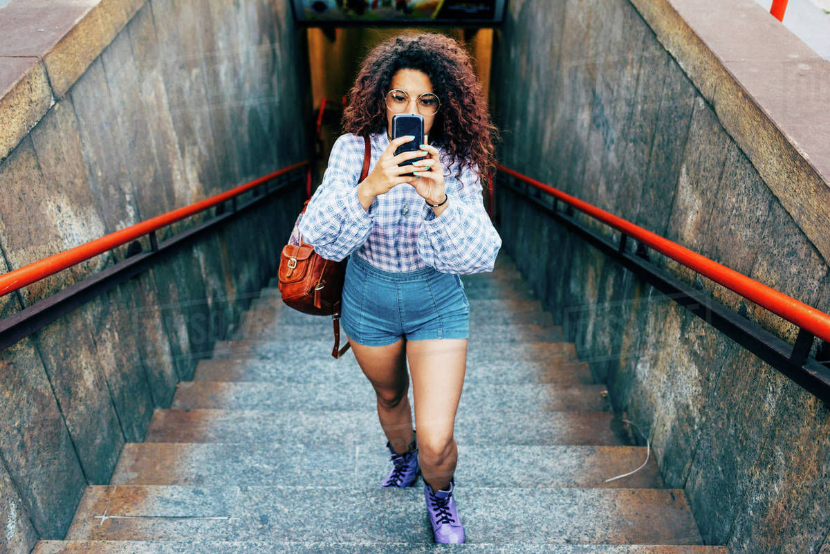 Woman coming up stairs and using mobile phone, Milan, Italy - Royalty ...