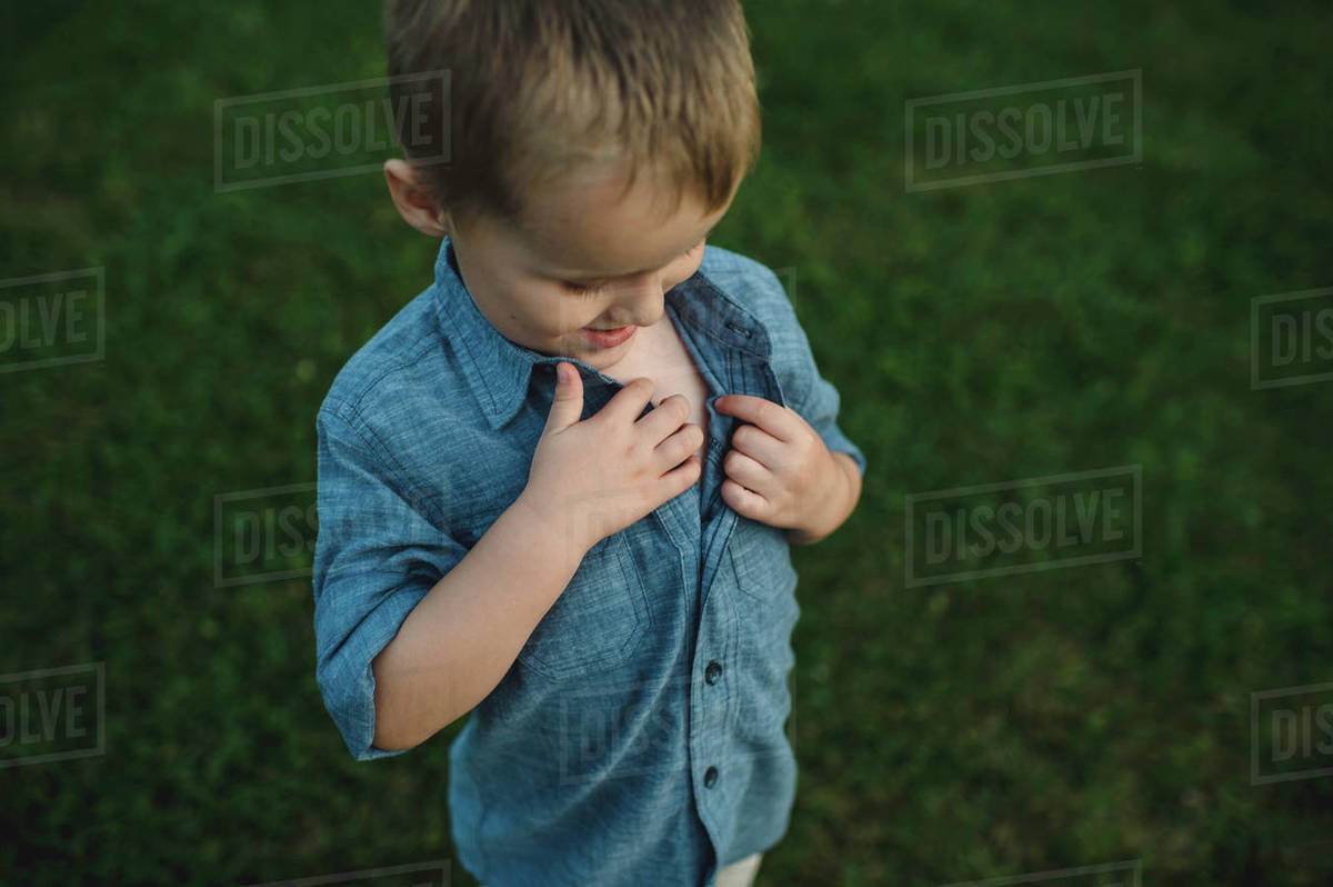 Boy unbuttoning shirt to investigate chest - Stock Photo - Dissolve