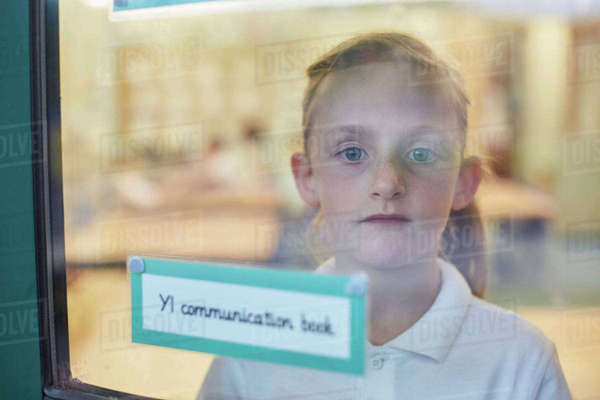 Portrait of schoolgirl looking through classroom window at primary ...