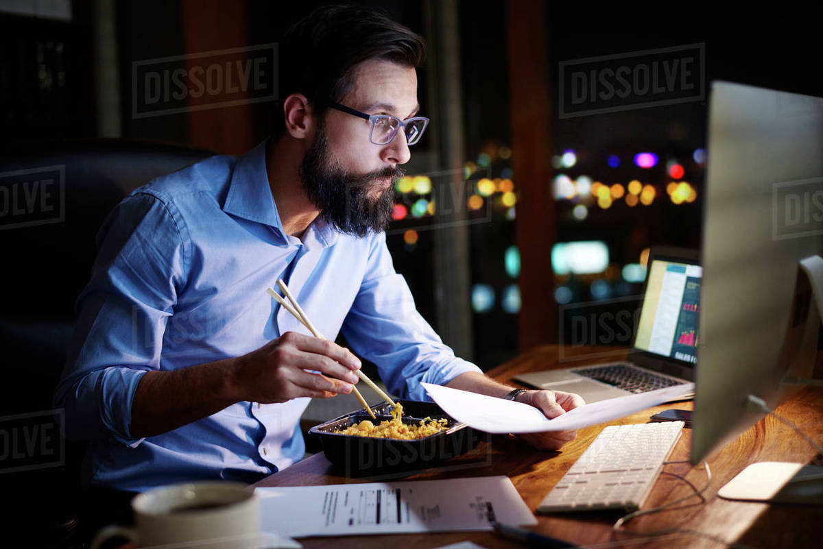 Young businessman looking at computer and eating takeaway at office ...