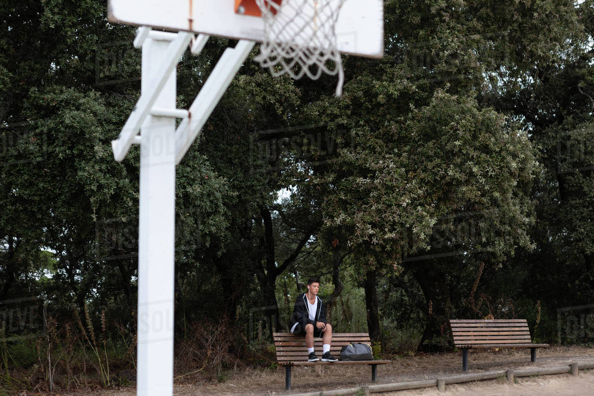 Male teenage basketball player sitting on park bench by basketball ...