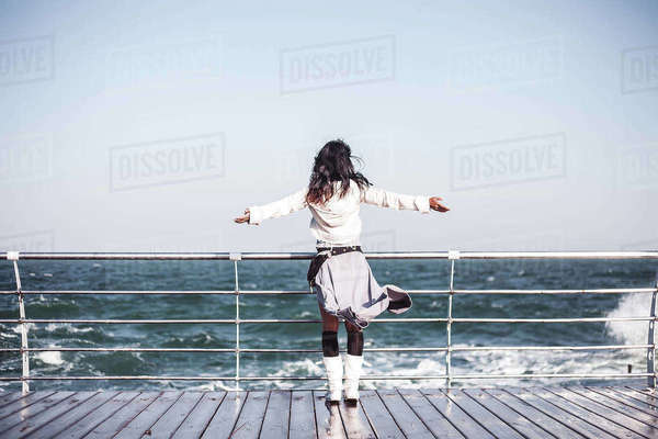 Mid adult woman looking out from pier with arms open, rear view, Odessa ...