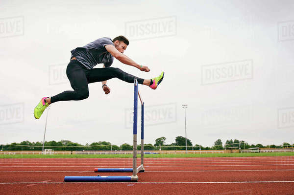 Athlete jumping over hurdle on running track - Royalty-free Stock Photo ...