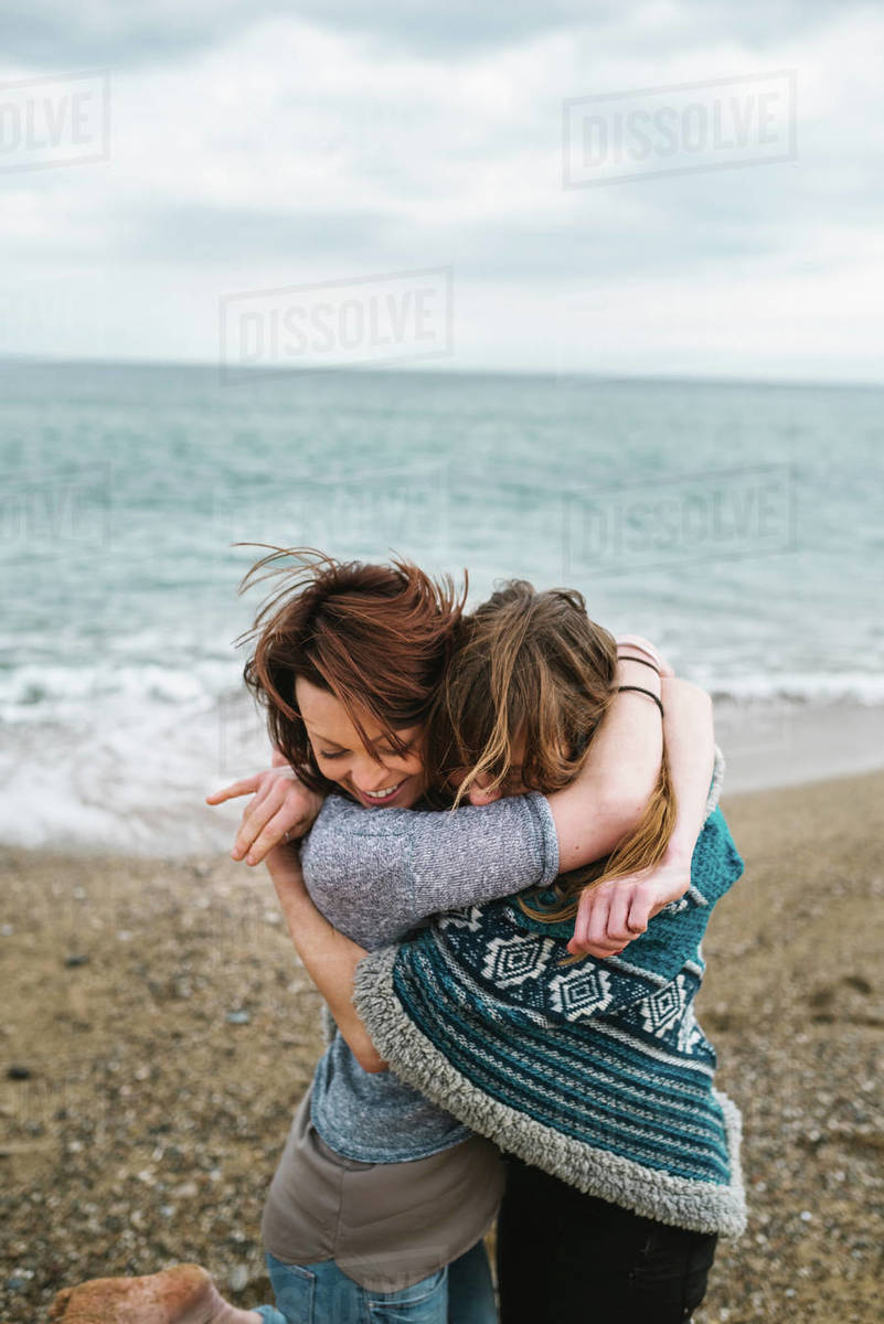 Two young adult female friends hugging on beach, Barcelona, Spain ...