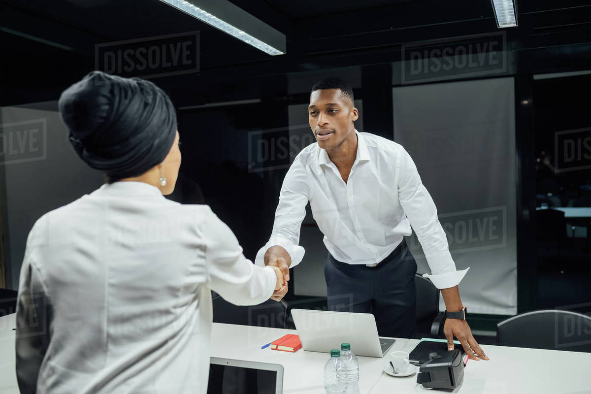 Businessman and woman shaking hands over conference table - Royalty ...