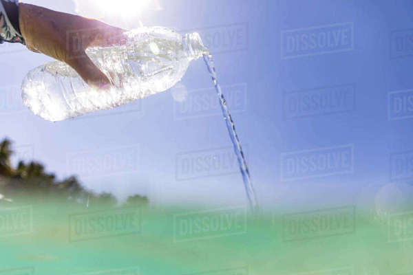 Woman pouring bottled water into sea - Royalty-free Stock Photo | Dissolve