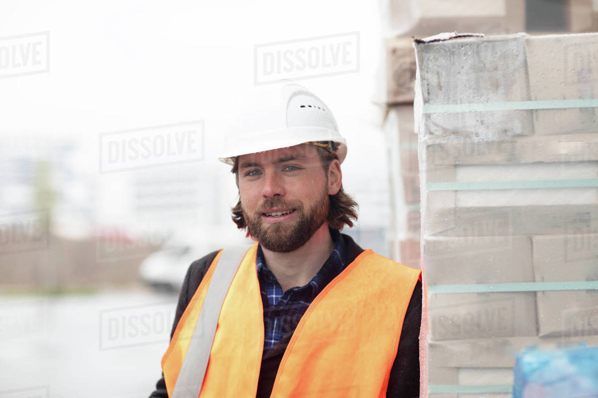 Mid adult male civil engineer leaning against stacked building material ...