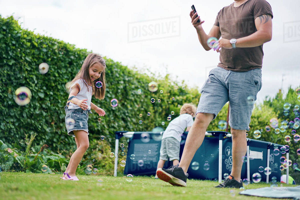 Father walking past children playing in garden - Royalty-free Stock ...