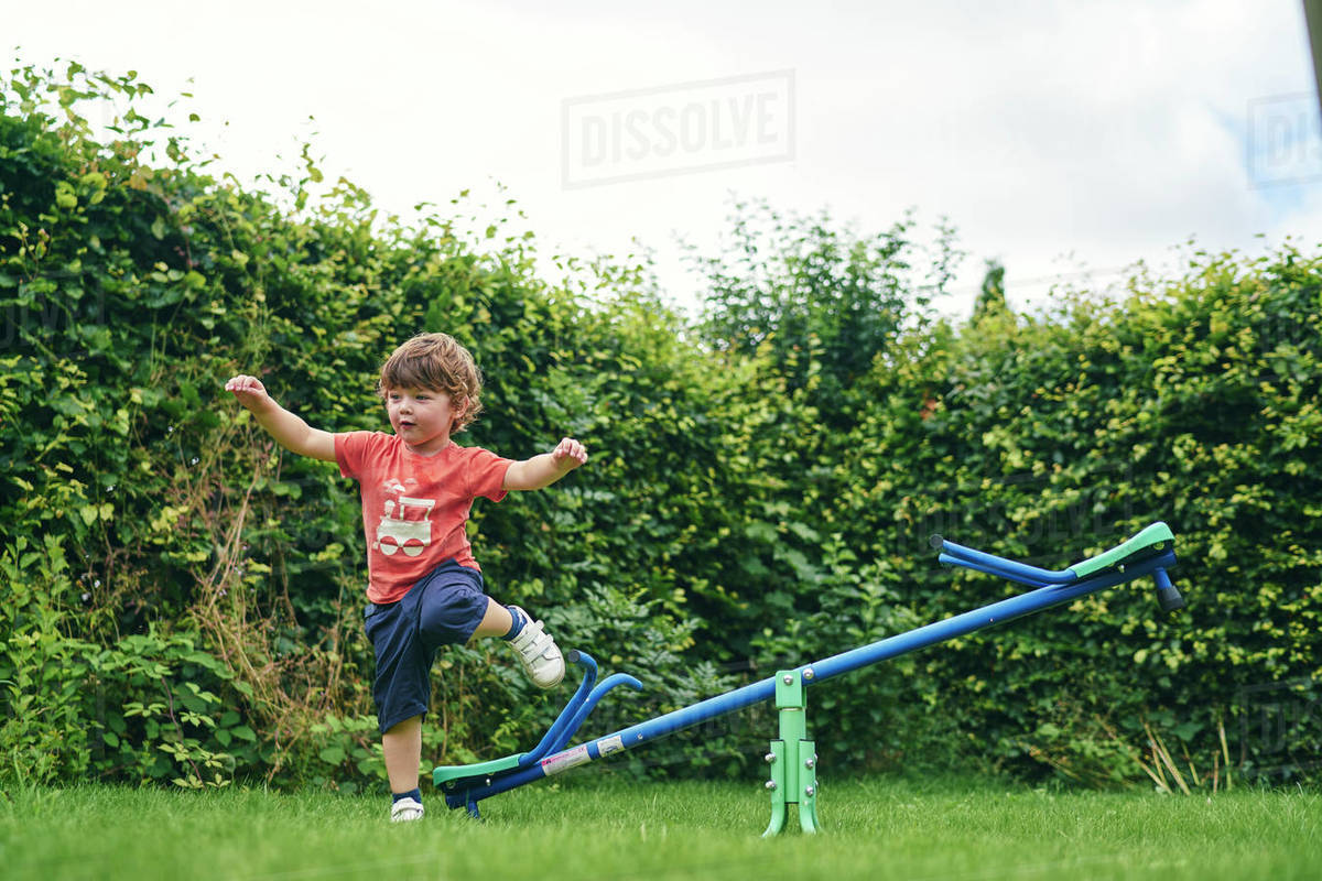 Boy hopping off toy seesaw in garden - Royalty-free Stock Photo | Dissolve