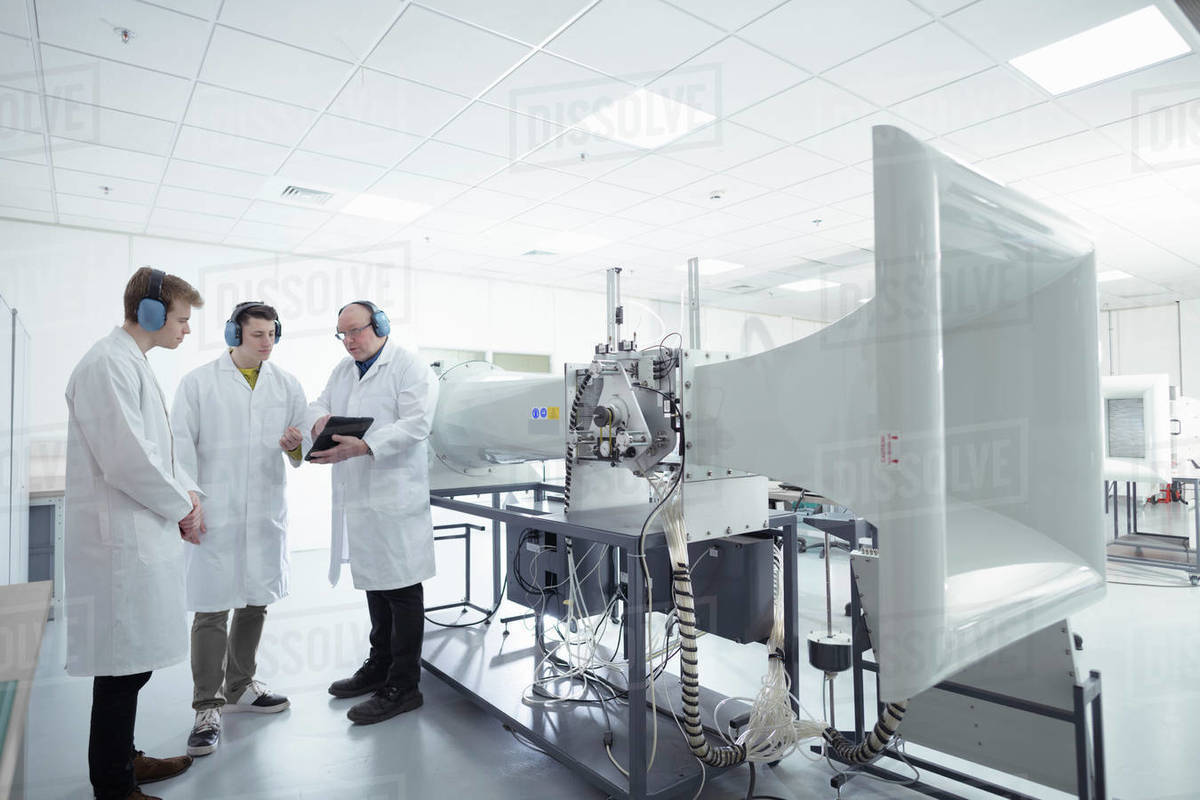Three male scientists wearing white lab coats performing experiment in ...