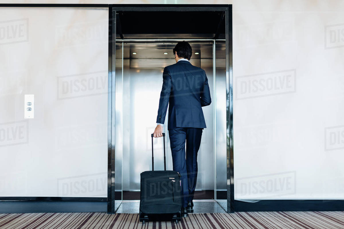 Businessman with wheeled luggage entering hotel lift - Royalty-free ...