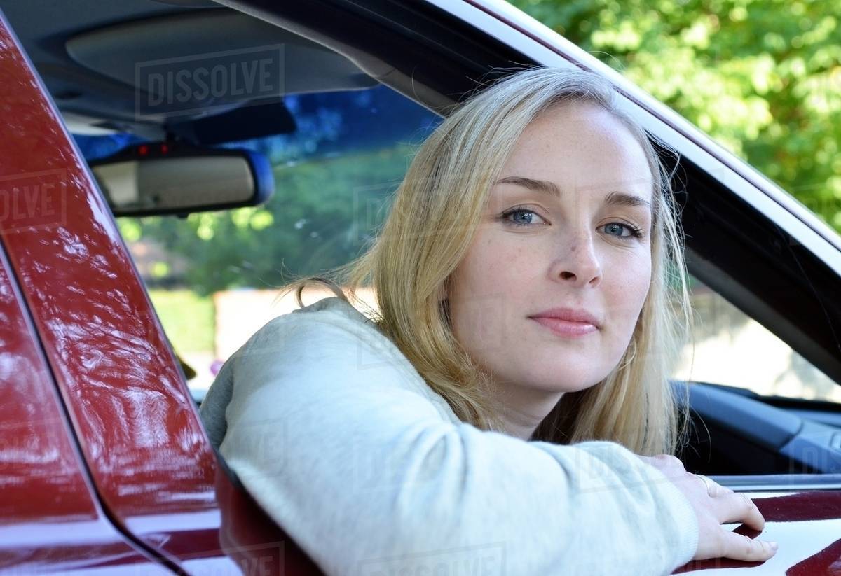 Portrait of young woman looking through car window - Stock Photo - Dissolve