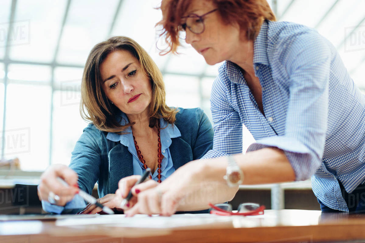 Two women, sitting at table, problem solving - Stock Photo - Dissolve