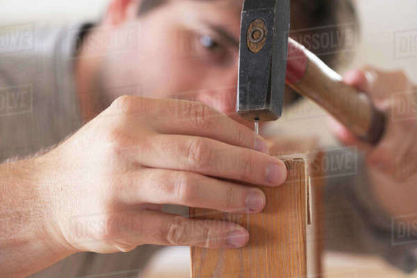 Young man knocking with hammer to a wood stick - Stock Photo - Dissolve