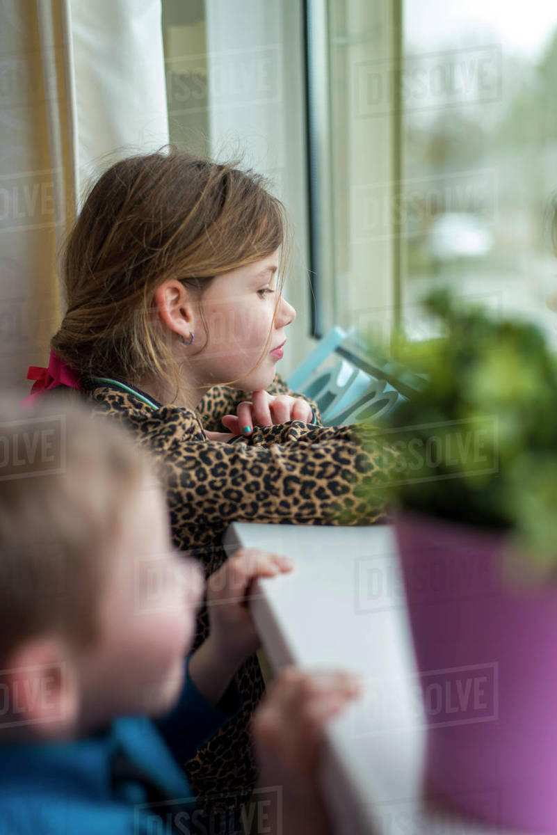 Thoughtful child gazing out a window with sibling nearby - Stock Photo ...