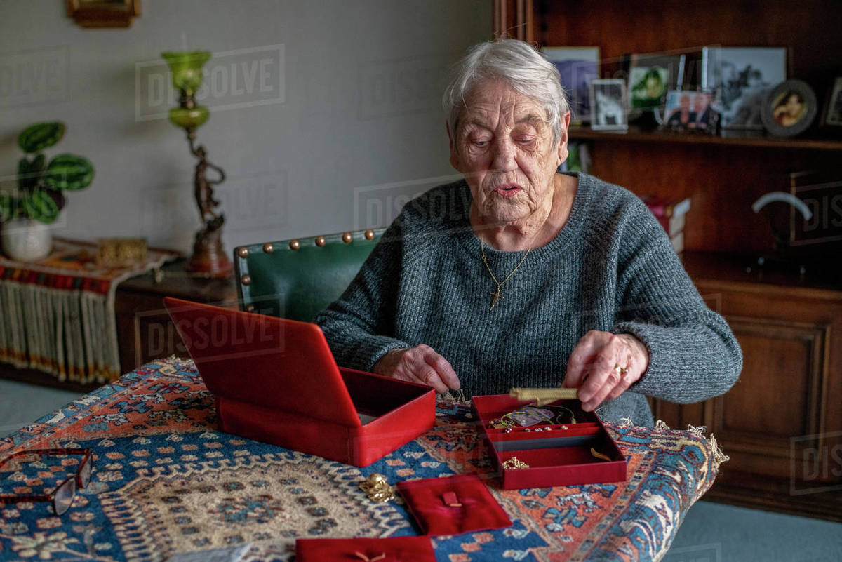 Elderly woman reminiscing with a box of old photographs in a cozy room ...