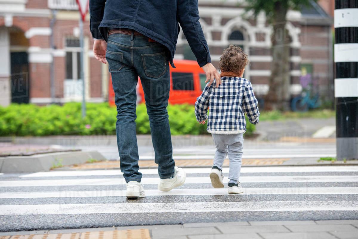 A parent and child holding hands while crossing the street. - Stock ...