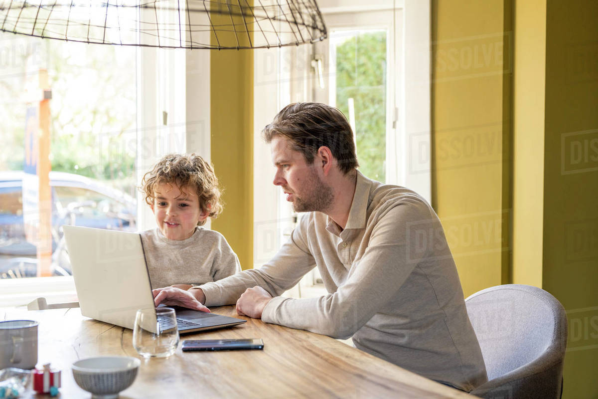 Adult teaching a young child to use a laptop at a home office setting ...