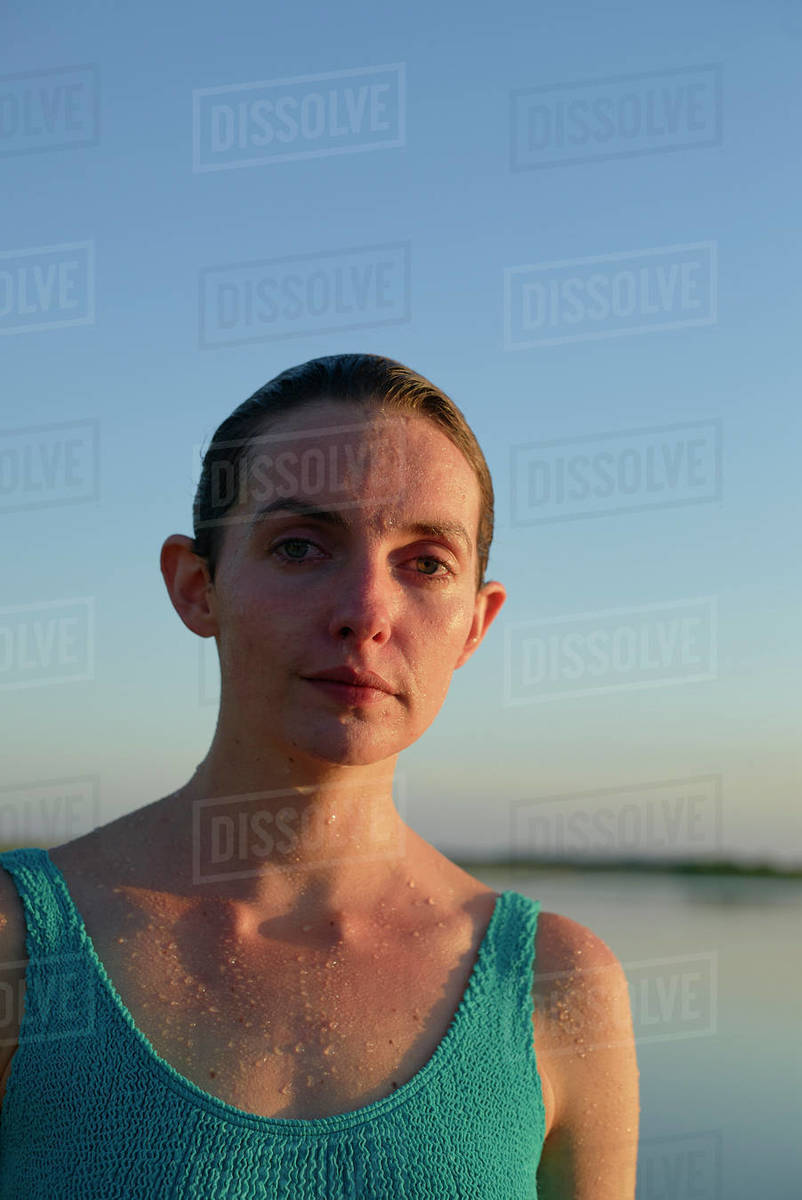 A woman stands by a lakeside at dusk, wearing a white one-piece ...