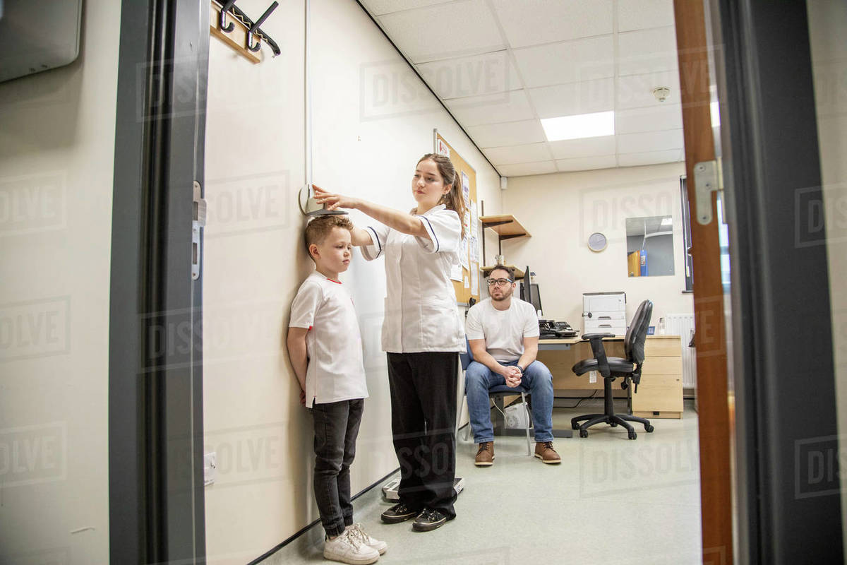 Child being measured during a medical check-up as father observes ...