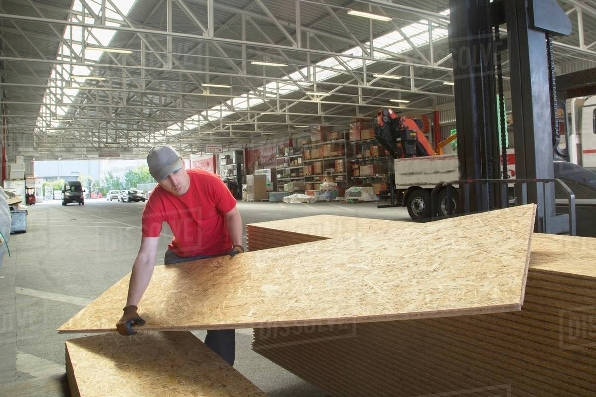 Warehouse worker lifting wooden boards in hardware store warehouse ...