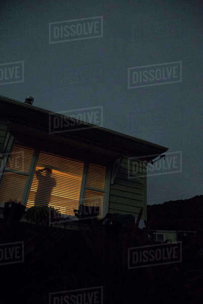Silhouette of a person standing behind a window with blinds at night ...