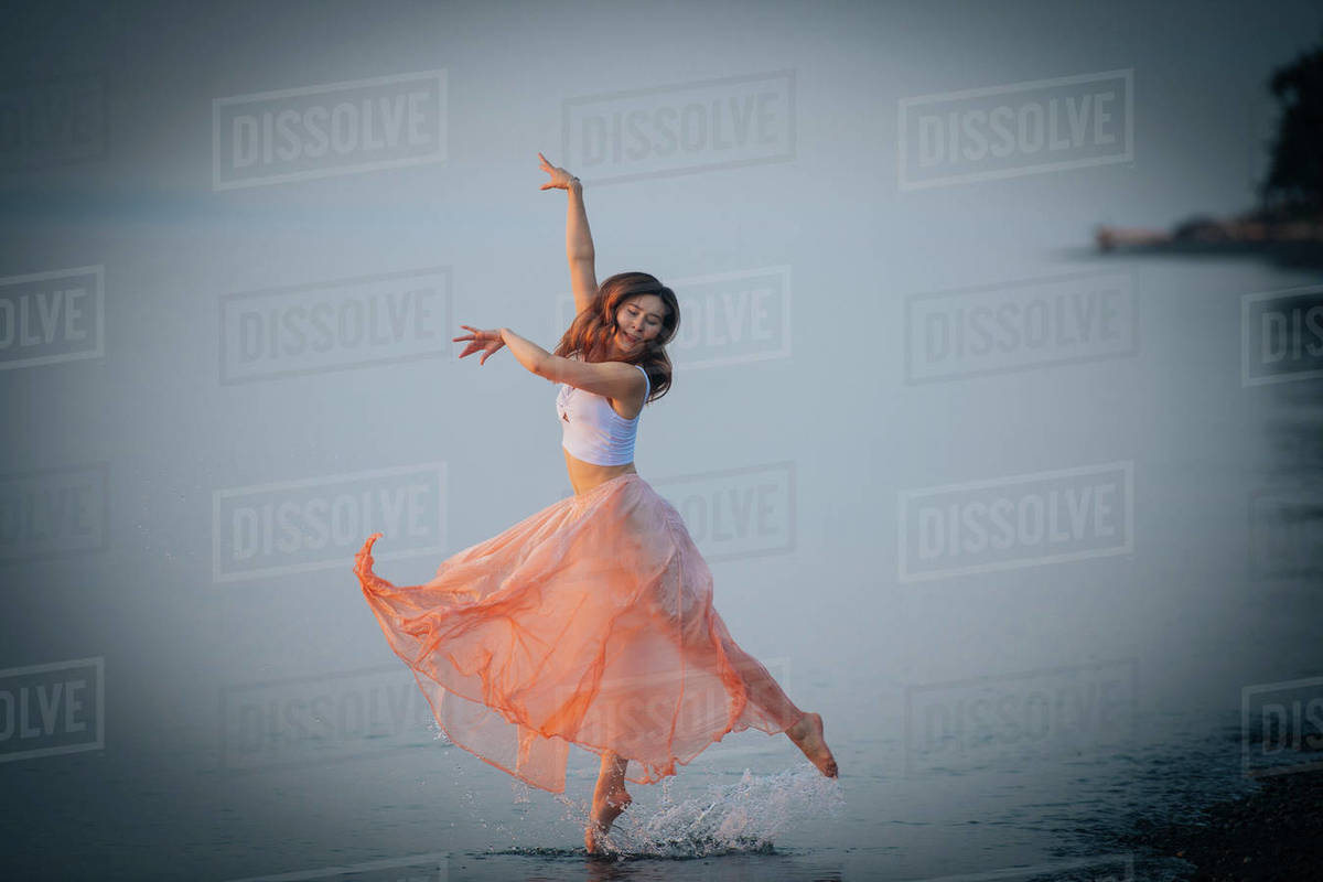 Ballerina dancing gracefully in shallow water at dusk, wearing a ...
