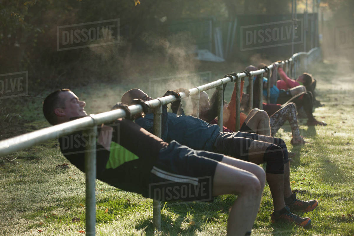 Group of people performing outdoor pull-up exercises on a row of bars ...