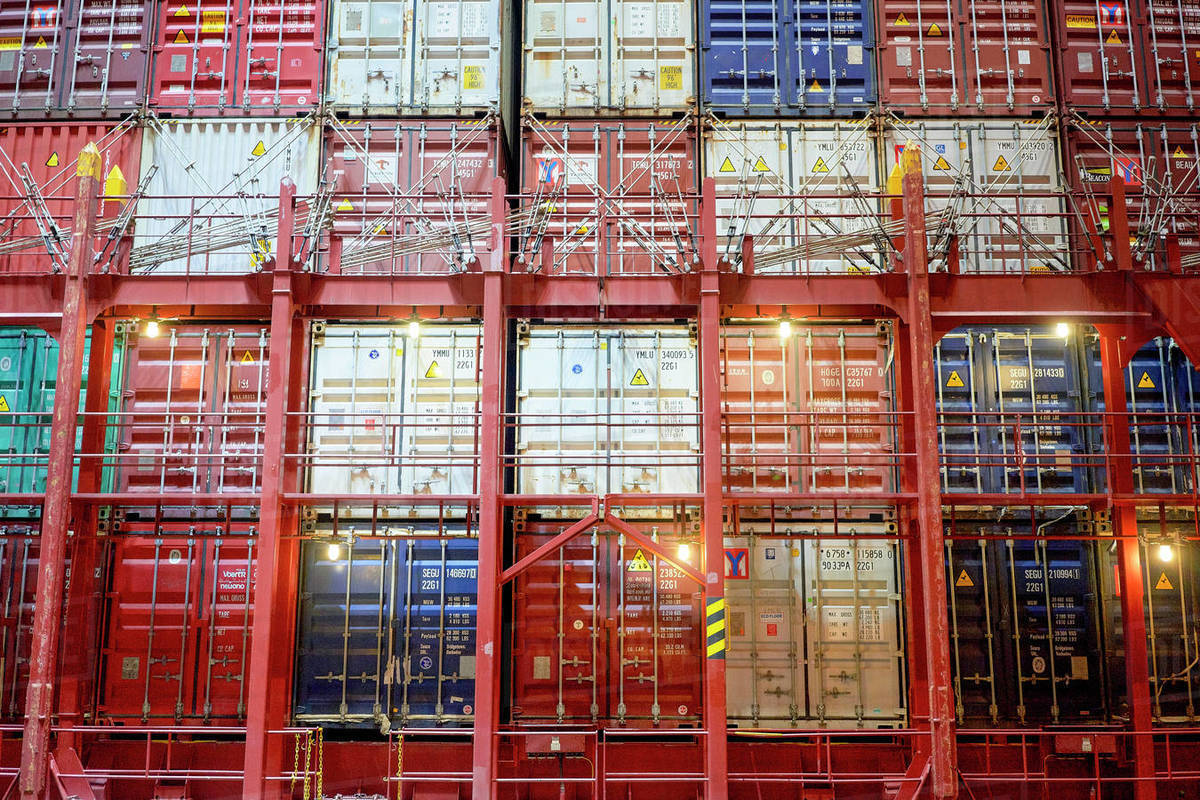 Worker inspecting a large stack of red shipping containers on a cargo ...