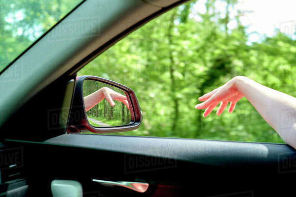 A person's arm reaching out of a car window is reflected in the side ...