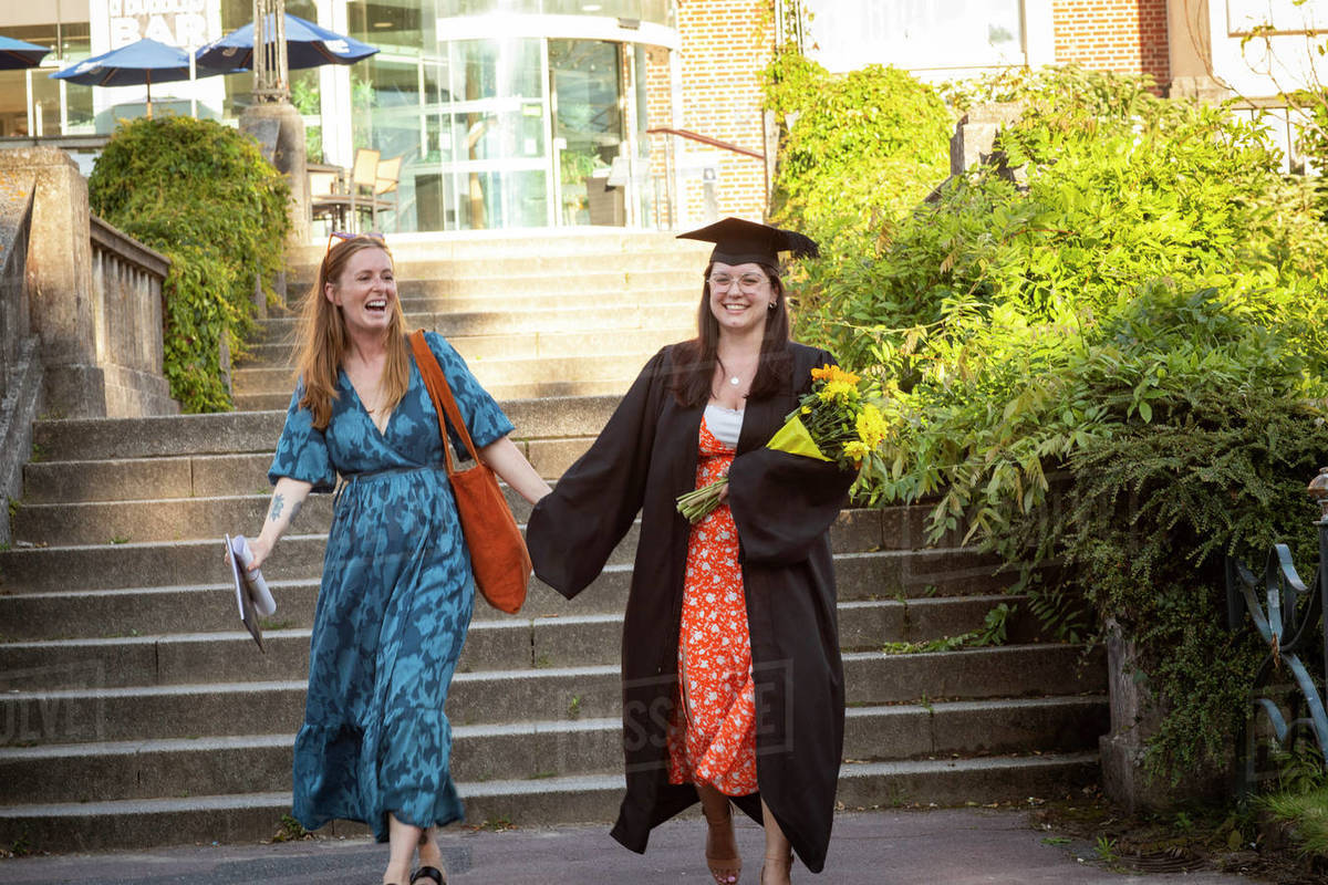 Two joyful women in graduation attire descending stairs with a ...