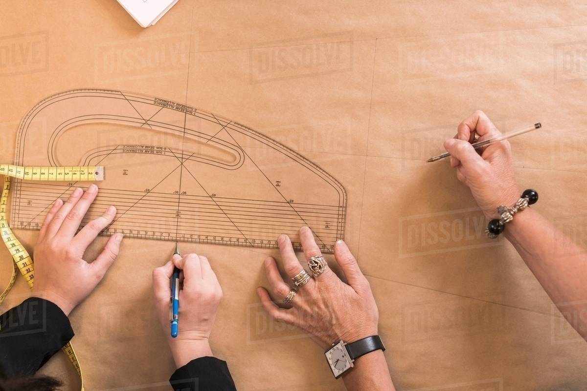 Overhead view of seamstresses hands drawing with curved ruler on ...