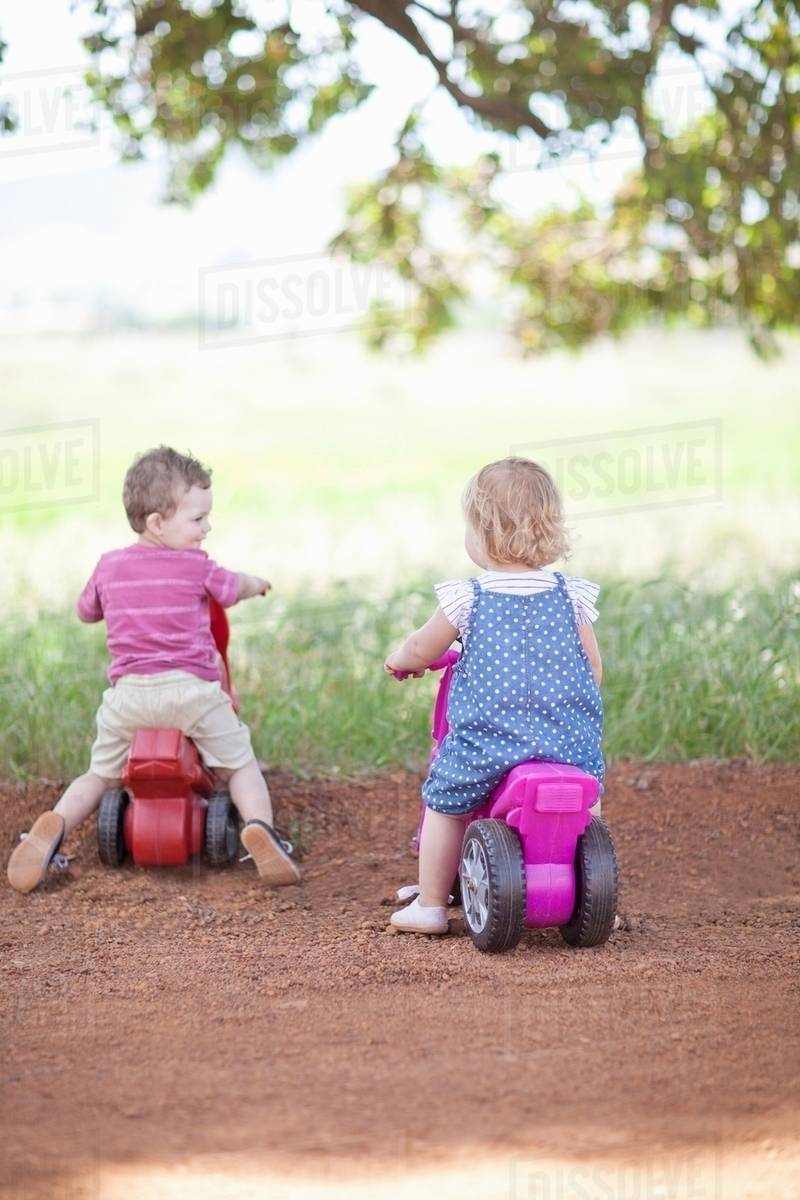 Toddlers riding toys on dirt road - Royalty-free Stock Photo | Dissolve