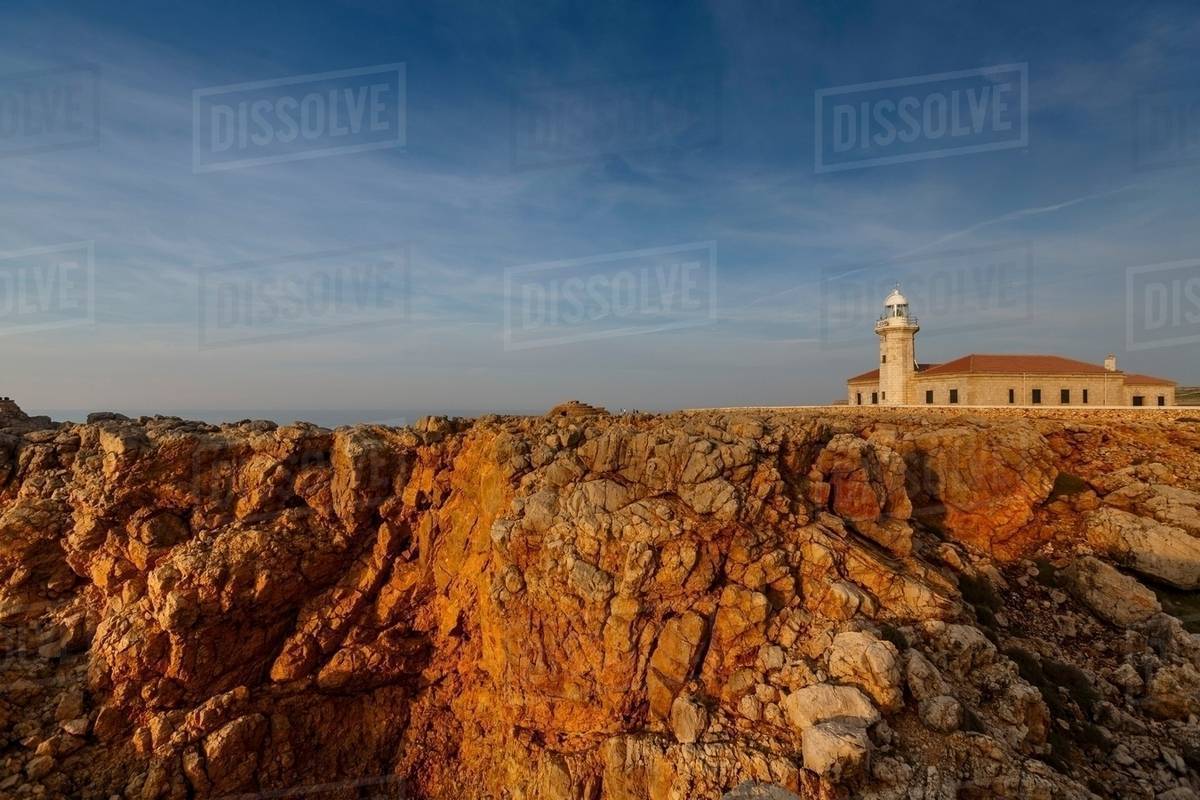 View of Punta Nati lighthouse on sunlit cliff, Menorca, Spain - Royalty ...