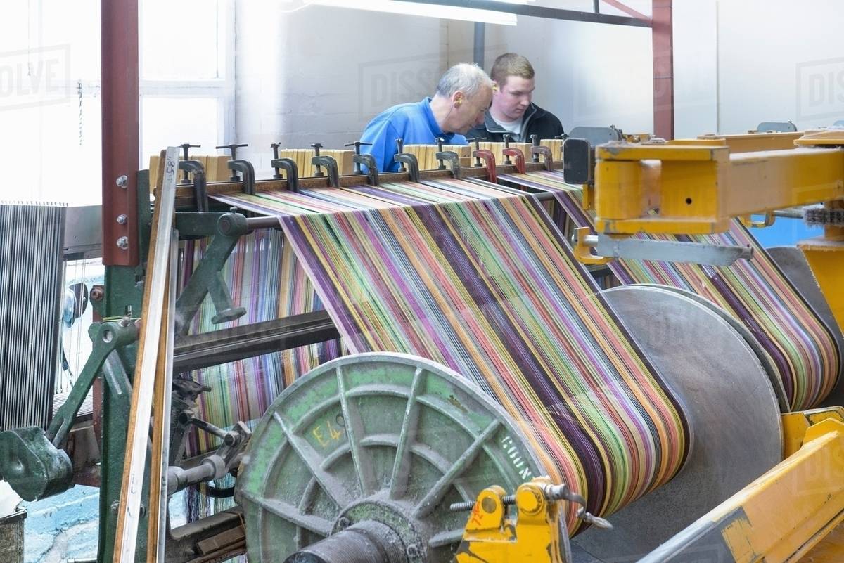 Workers using multicoloured thread on industrial loom in textile mill ...