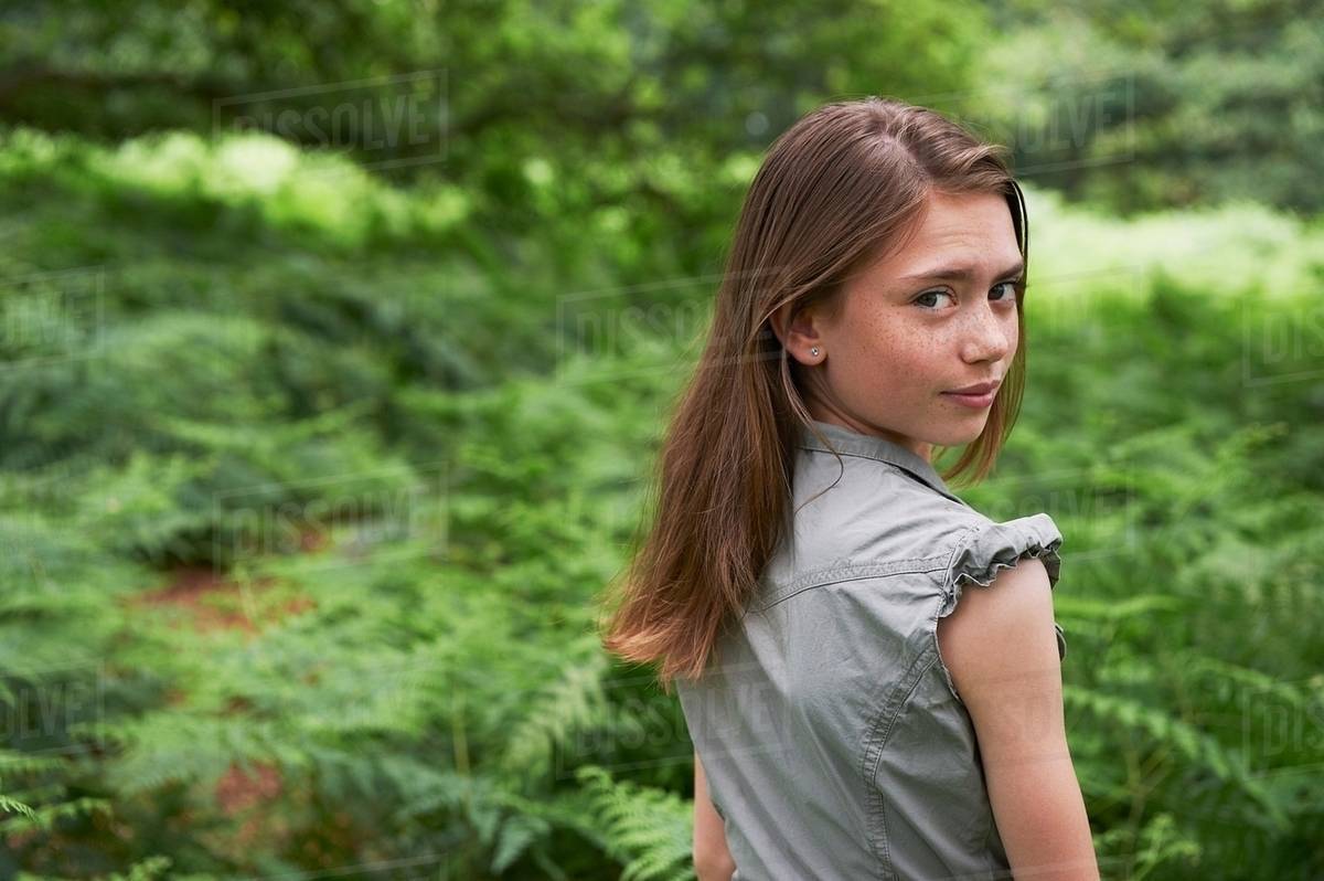 Teenage girl looking over shoulder in forest - Stock Photo - Dissolve