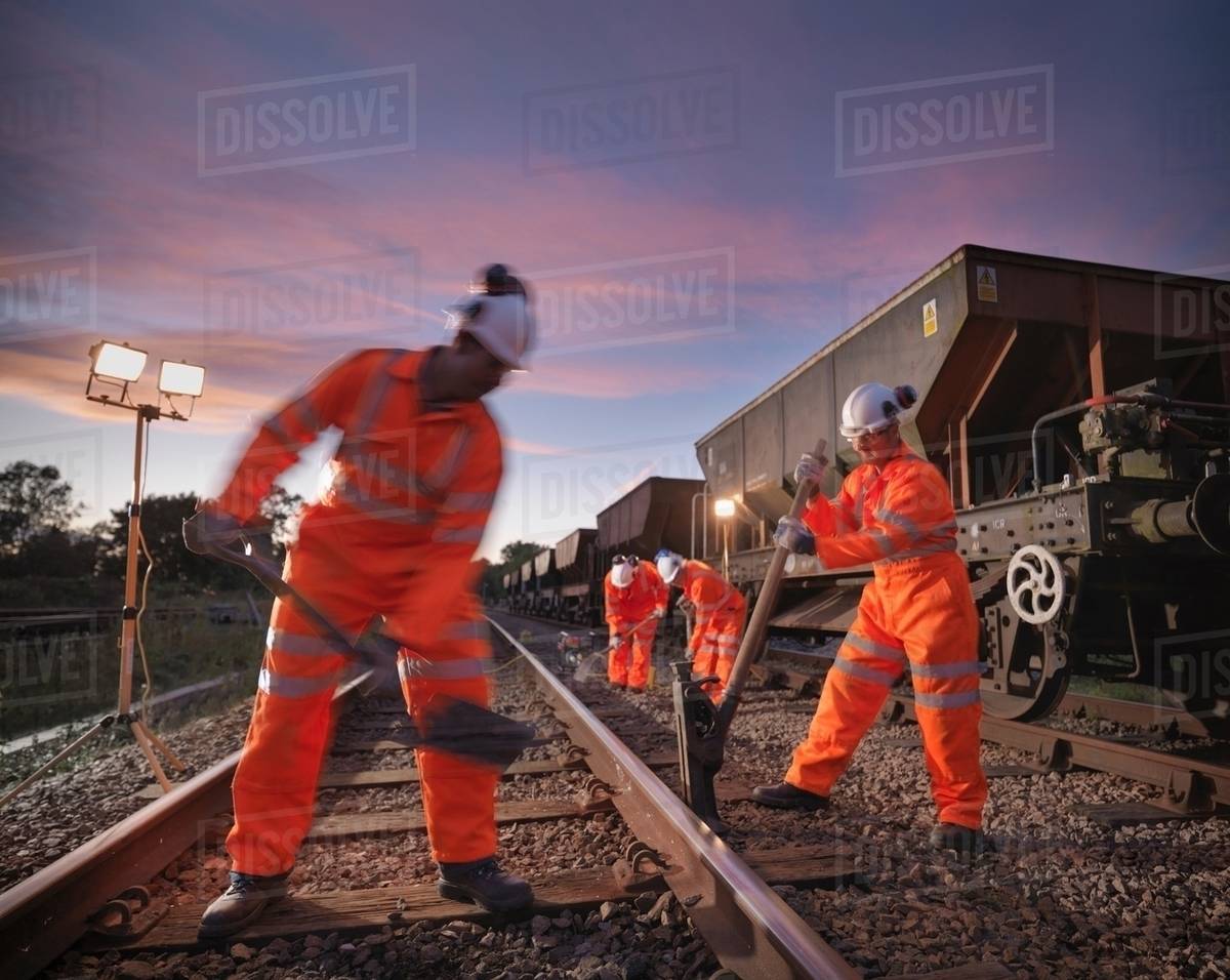 Railway workers with spade and tools working on railway tracks at night ...