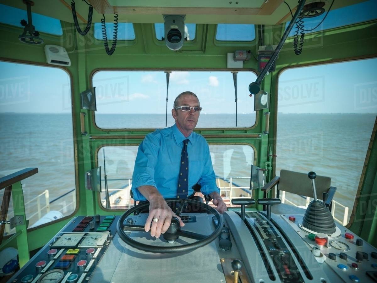 Captain steering in wheelhouse of tugboat at sea - Stock Photo - Dissolve