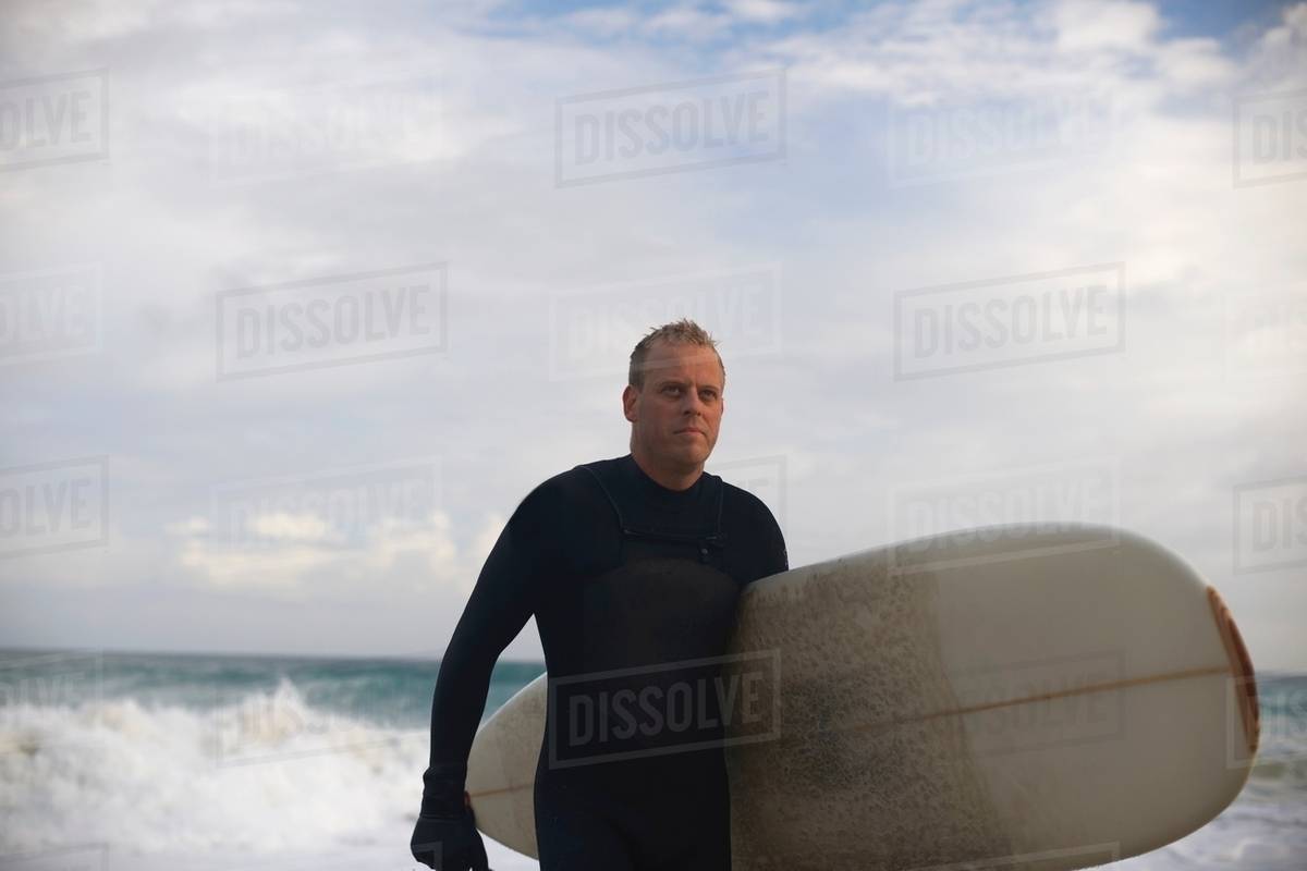 Surfer carrying board on beach - Royalty-free Stock Photo | Dissolve