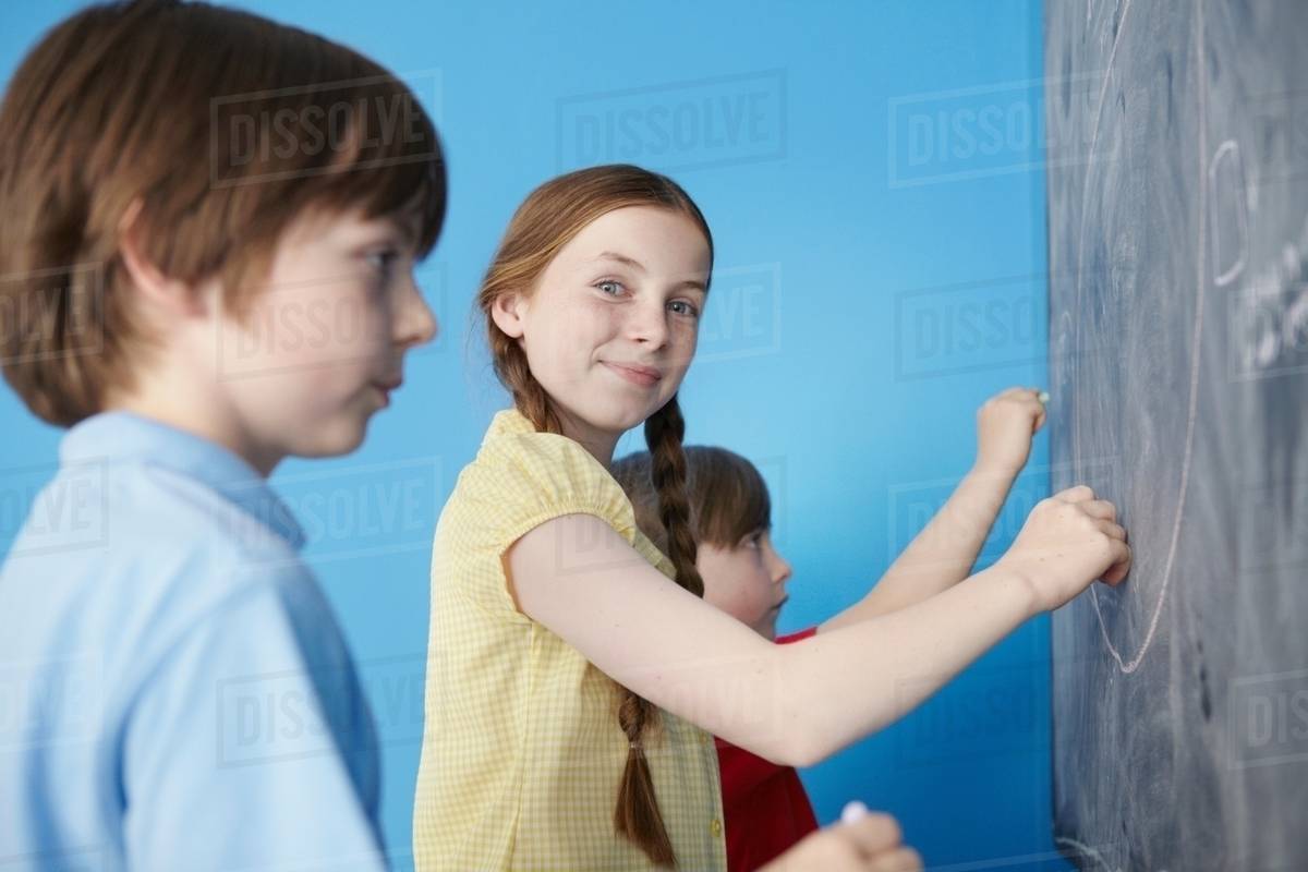 Children writing on blackboard, blue background - Stock Photo - Dissolve