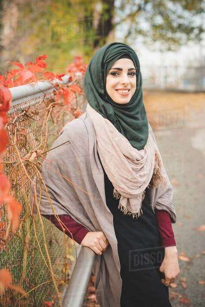 Portrait of young woman leaning against railing on park path - Stock ...