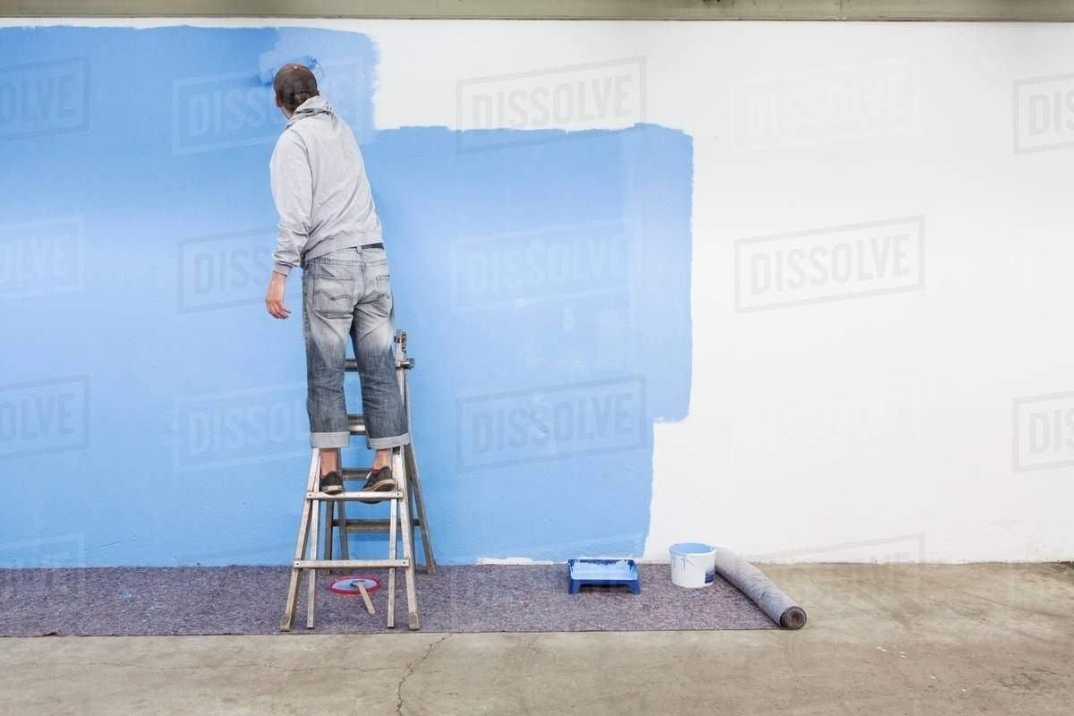 Rear view of man painting wall blue - Royalty-free Stock Photo | Dissolve