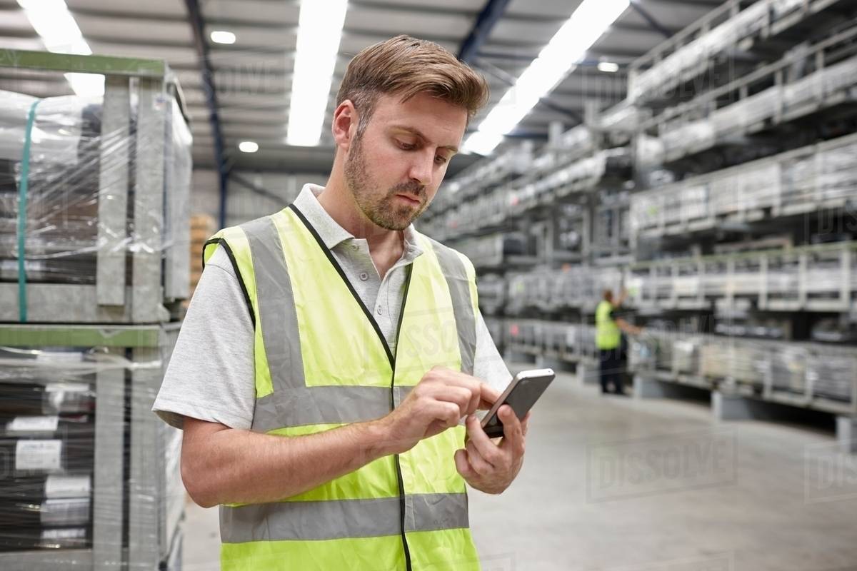 Portrait of worker using mobile phone in engineering warehouse ...