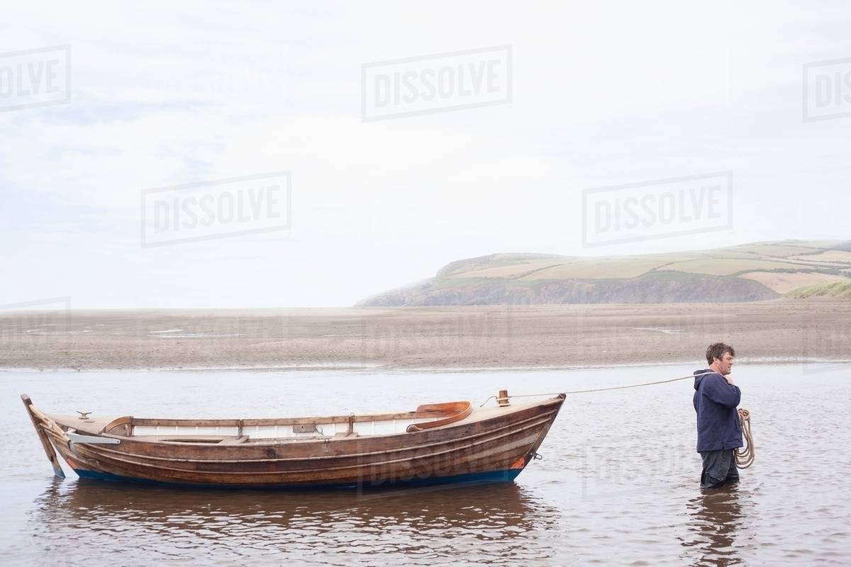 Man pulling rowing boat through water, Wales, UK - Stock Photo - Dissolve