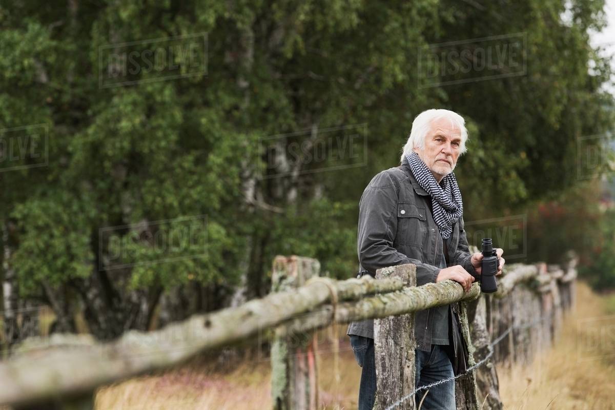 Senior man leaning on wooden fence with binoculars - Royalty-free Stock ...