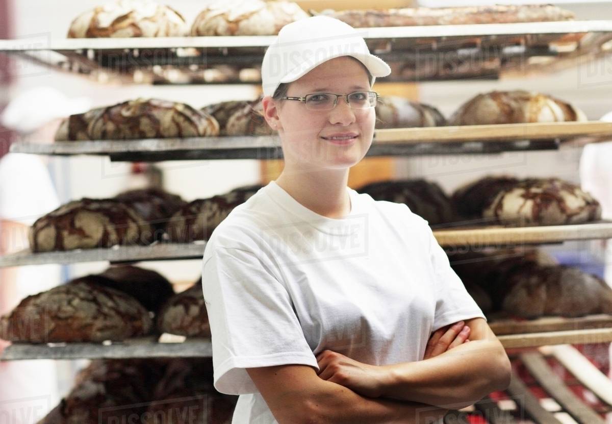 Baker standing in front of bread on shelves with arms folded - Royalty ...