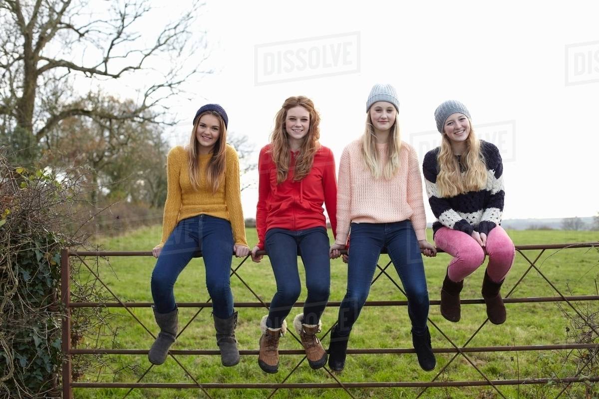 Four teenage girls sitting on gate - Stock Photo - Dissolve