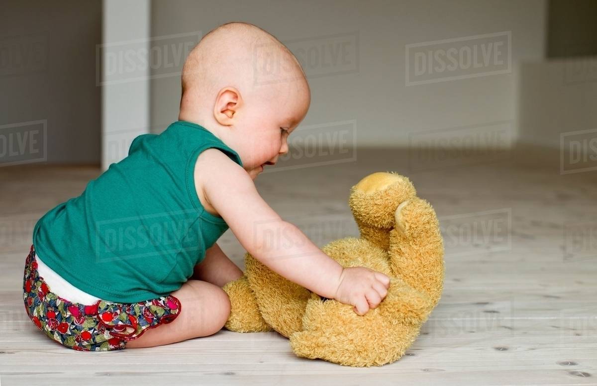 Baby girl playing with teddy bear on floor - Stock Photo - Dissolve