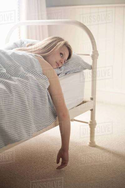 Teenage girl lying in bed with arm dangling - Stock Photo - Dissolve