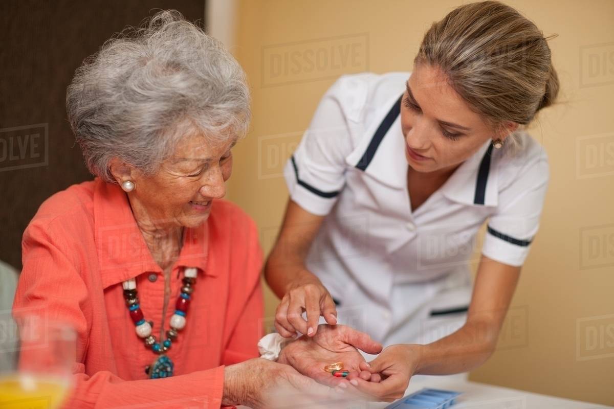 Care assistant handing medication to senior woman - Royalty-free Stock ...
